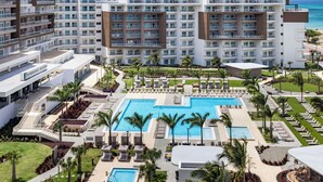 Um hotel com vários andares, área central da piscina com espreguiçadeiras e vista para o oceano.