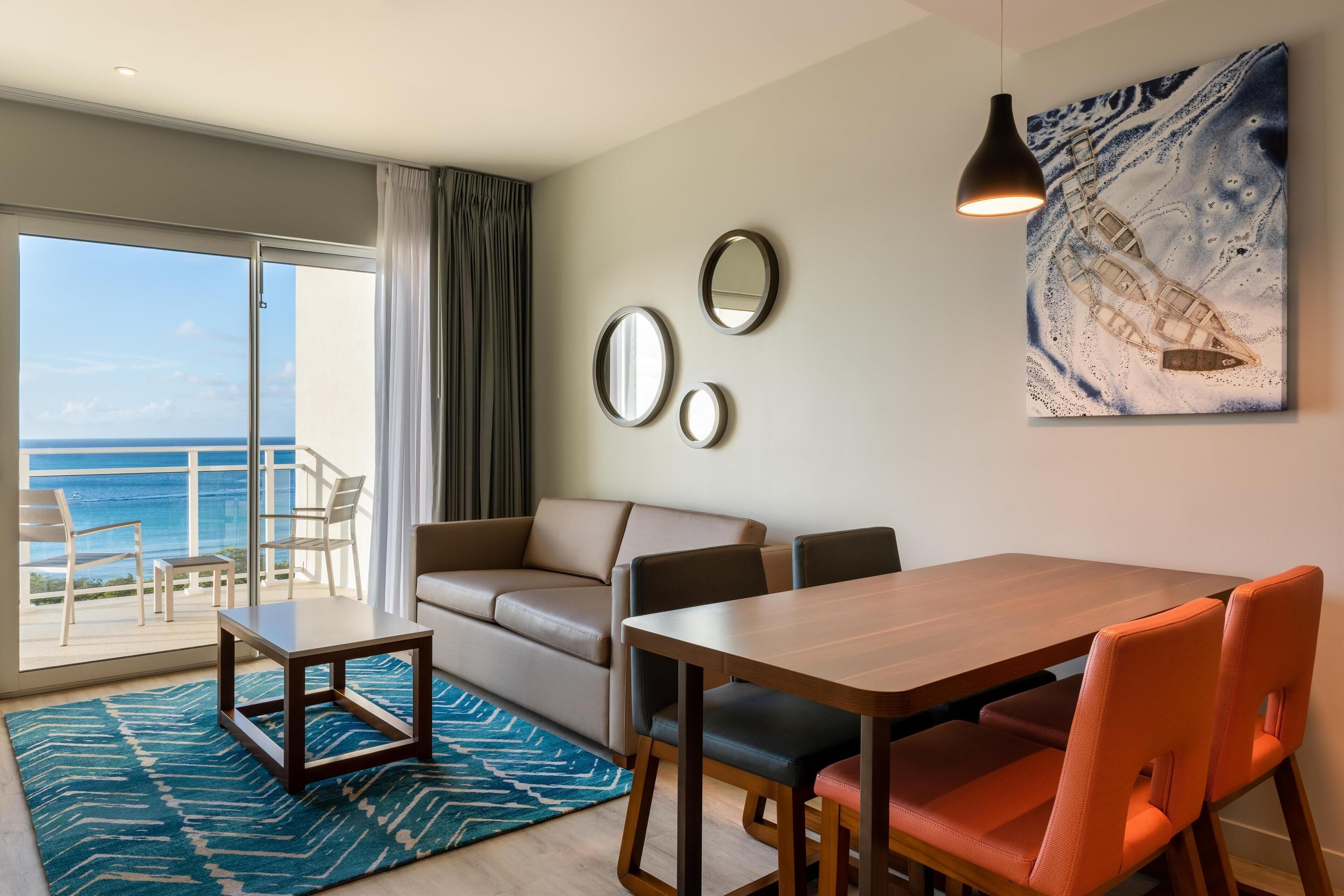 Quarto de hotel moderno com varanda, uma mesa de jantar e um sofá.
