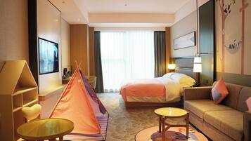 Quarto de hotel com cama, sofá, mesa pequena, cadeira, tenda e televisão.
