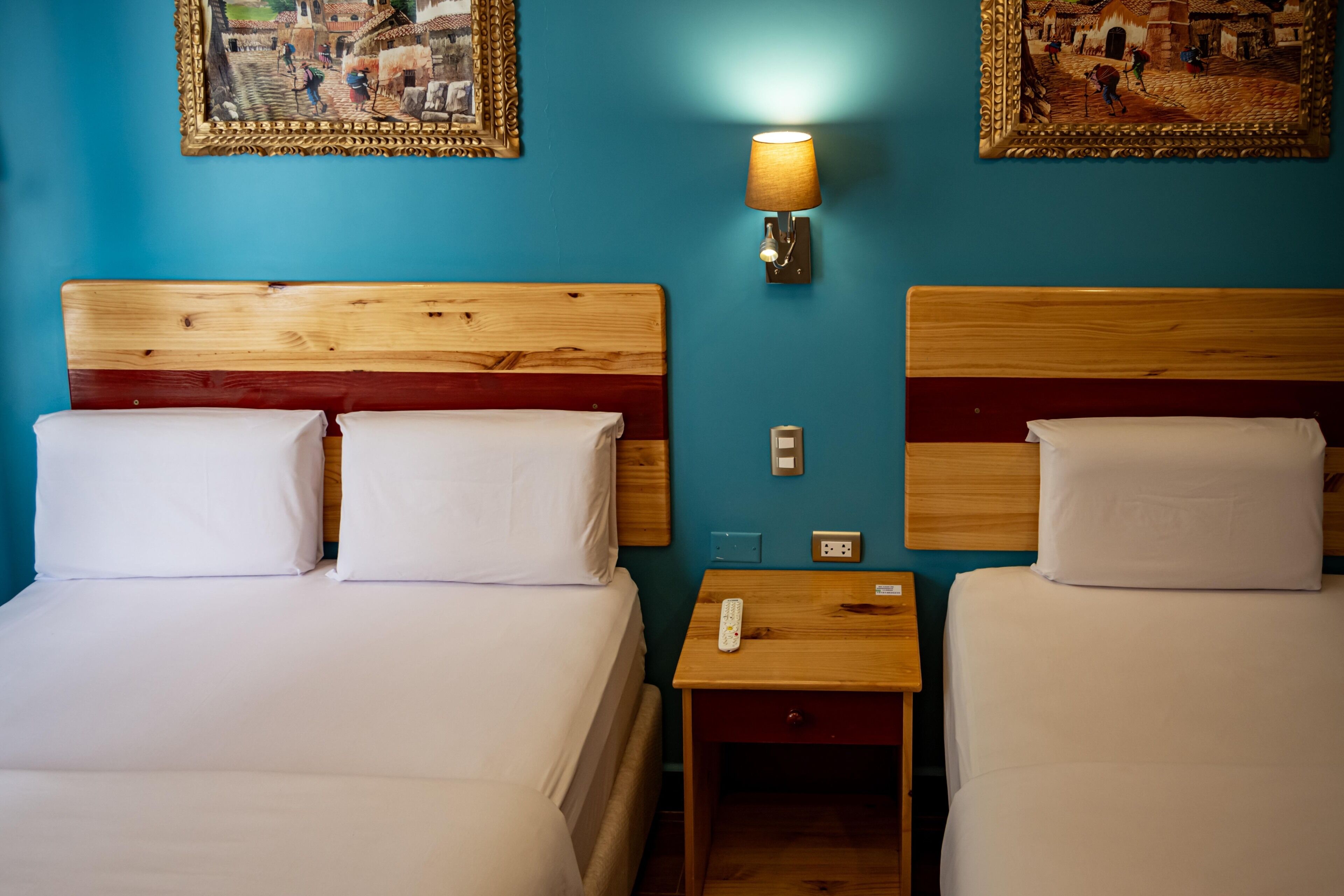Quarto de hotel com duas camas, uma mesa de cabeceira, um abajur e duas imagens emolduradas na parede.