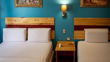 Quarto de hotel com duas camas, uma mesa de cabeceira, um abajur e duas imagens emolduradas na parede.