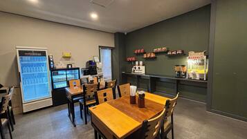 Interior de restaurante com mesa e cadeiras de madeira, um dispensador de bebidas e uma máquina de café.