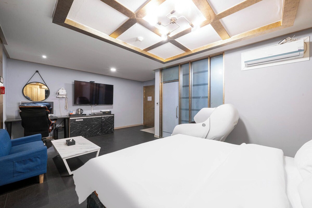 Quarto de hotel moderno com cama, escrivaninha, cadeira, televisão e uma grande janela.