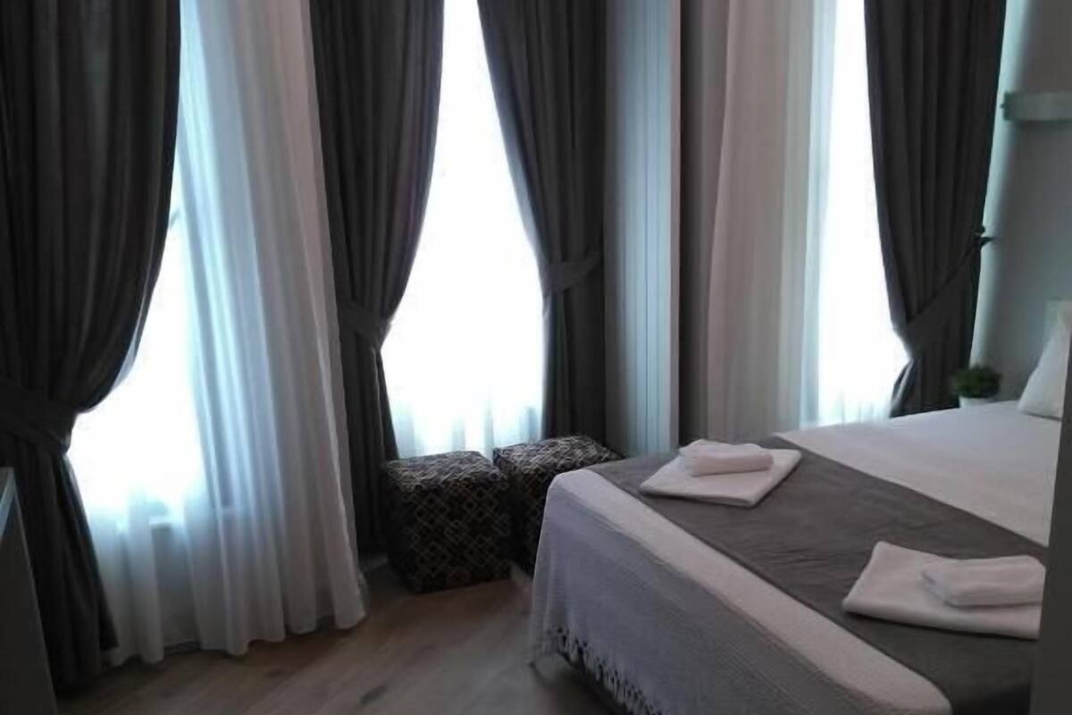 Quarto de hotel com cama, um pequeno sofá e uma janela grande com cortinas.