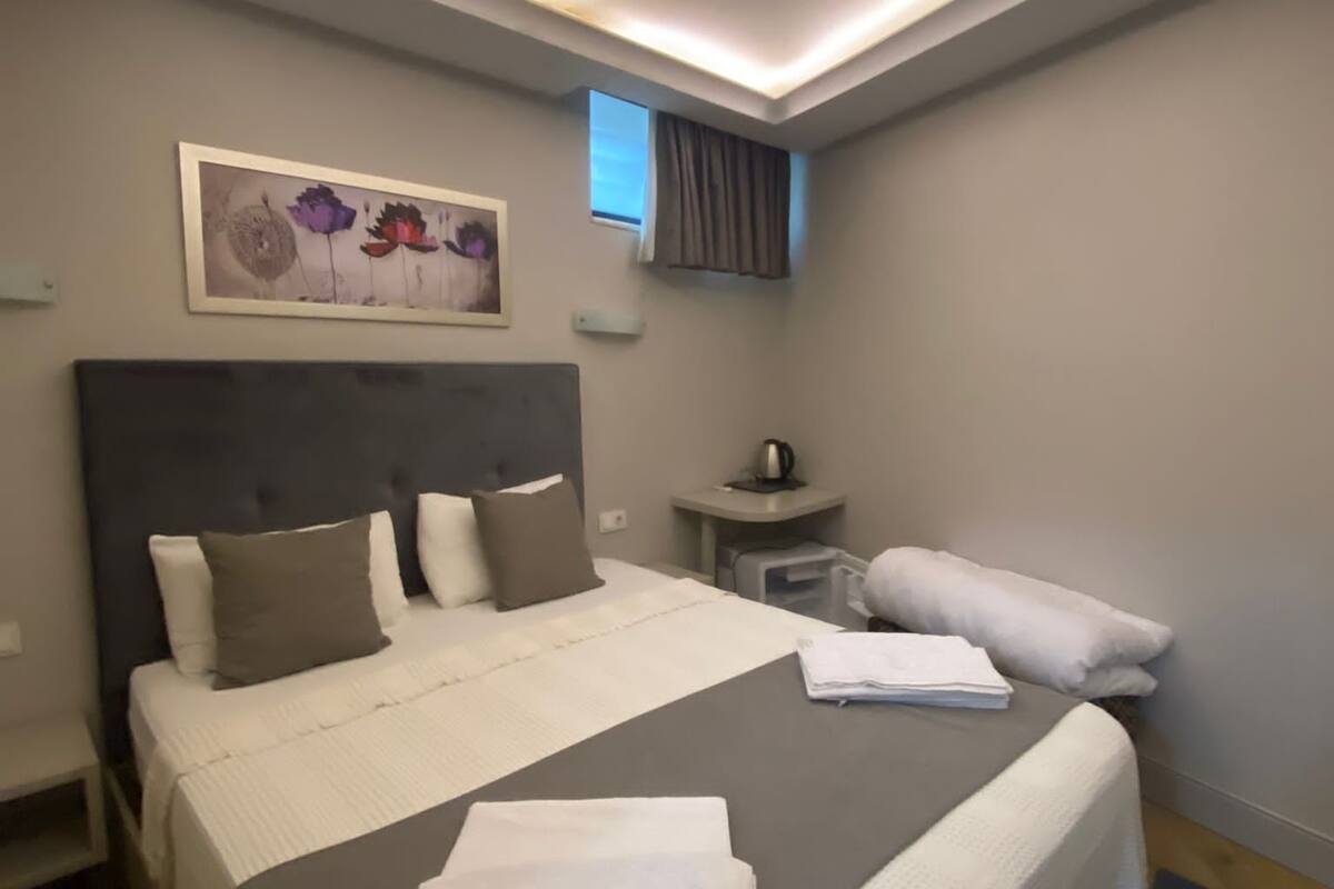 Quarto de hotel moderno com uma cama grande, uma mesinha de cabeceira, uma pequena escrivaninha e um lustre.