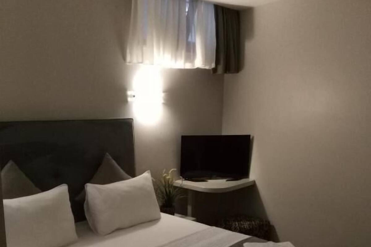 Quarto de hotel com uma cama, uma televisão sobre uma mesinha e uma janela com cortinas.