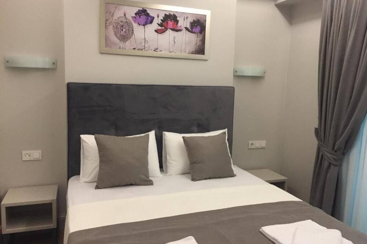 Cama bem arrumada com cabeceira escura, duas mesas de cabeceira e uma obra de arte na parede acima da cama.