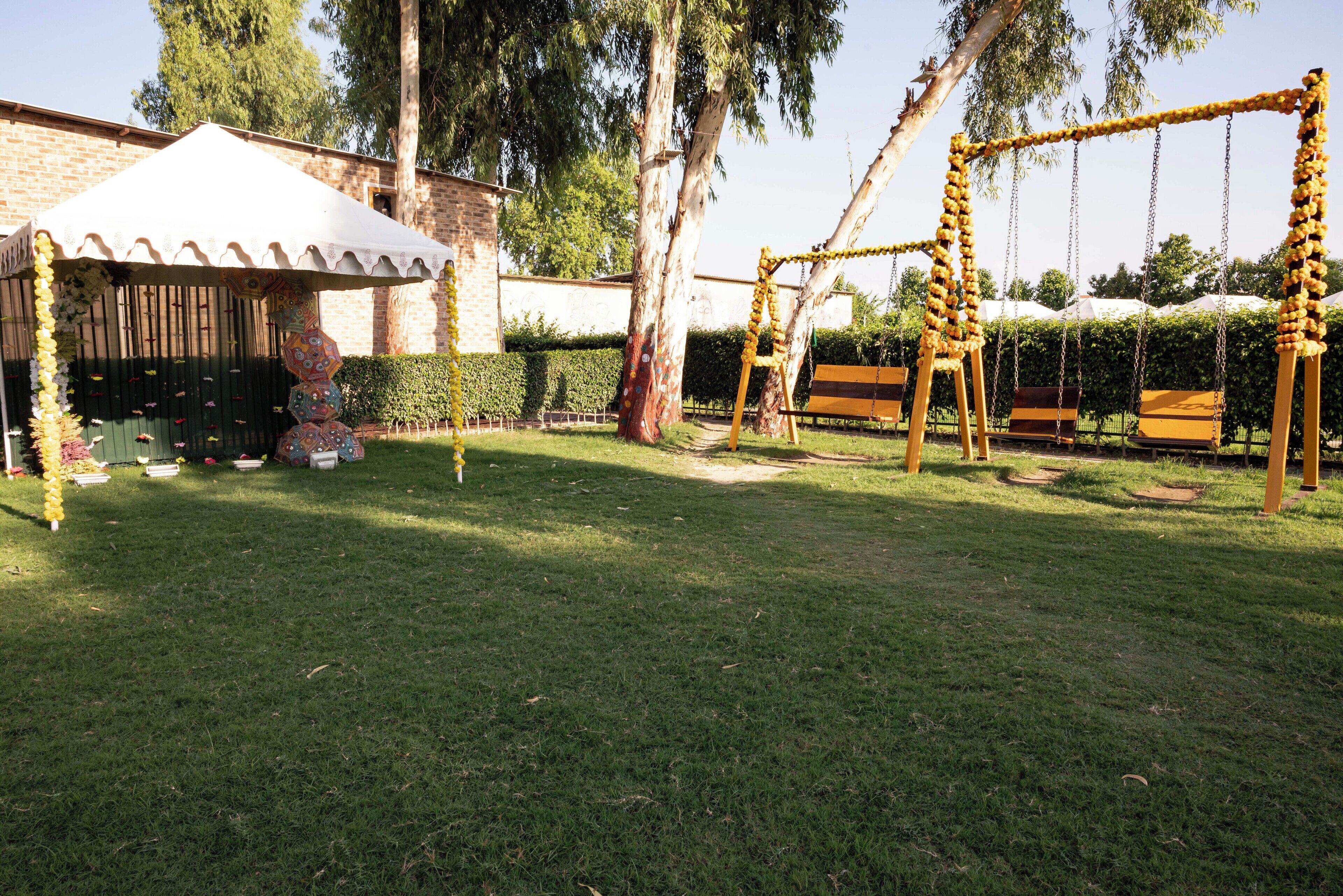 Um jardim com baloiço, área de estar coberta e um edifício ao fundo.