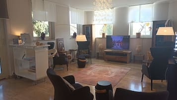 Uma sala de estar moderna com uma televisão de tela plana, assentos confortáveis e um lustre decorativo.