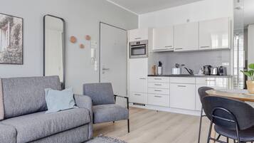 Uma sala de estar moderna com um sofá cinzento, uma poltrona pequena e uma área de jantar com mesa e cadeiras de madeira.