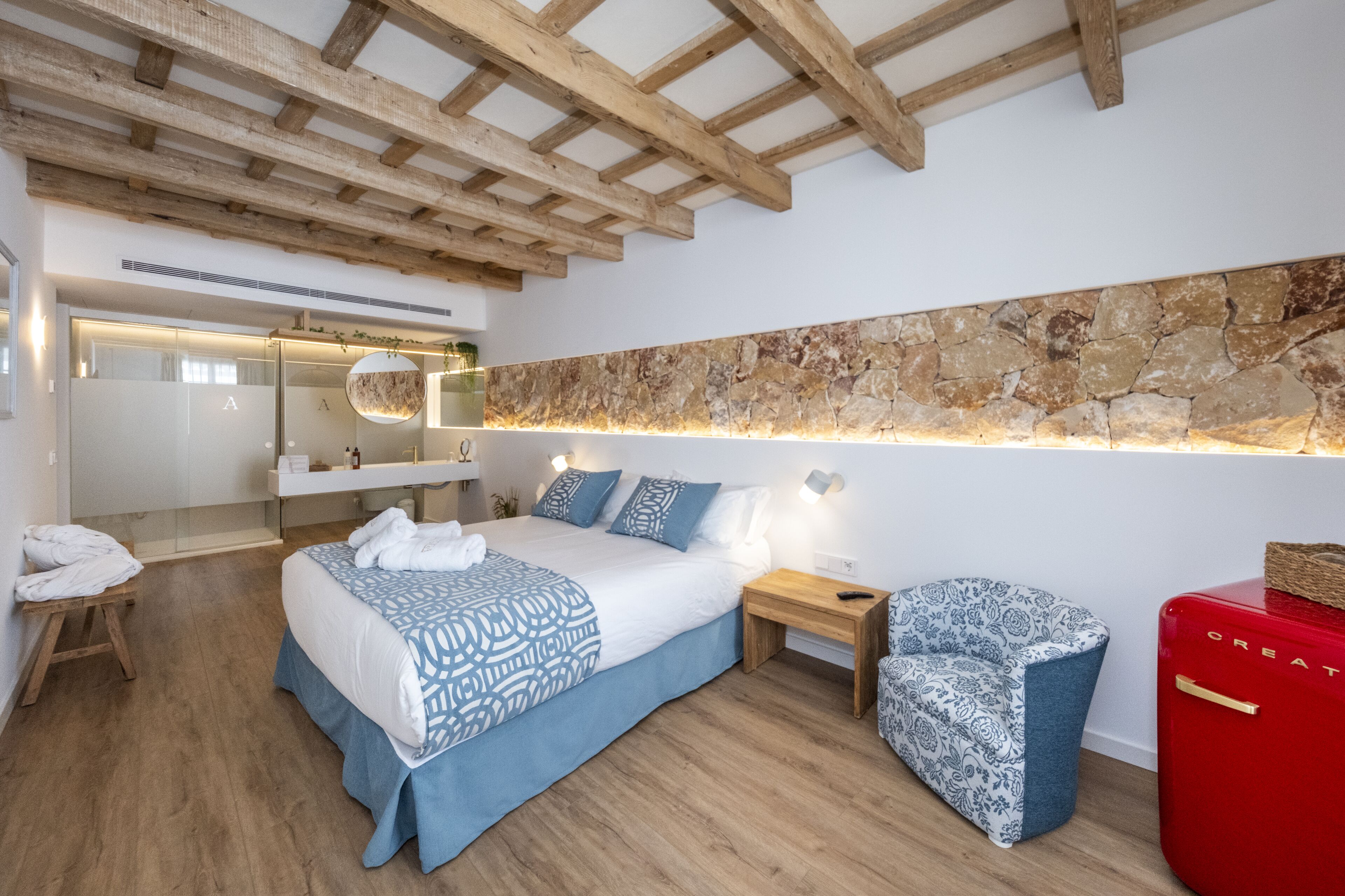 Quarto moderno com uma cama grande, mesa de cabeceira, uma cadeira e uma mala vermelha.