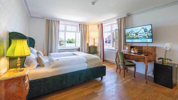 Quarto de hotel com cama, escrivaninha, cadeira, televisão e janela com cortinas.