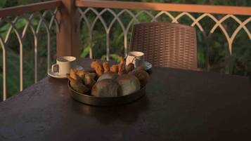 Uma mesa com uma tigela de pão e uma chávena numa varanda com grades de metal e vista para árvores.