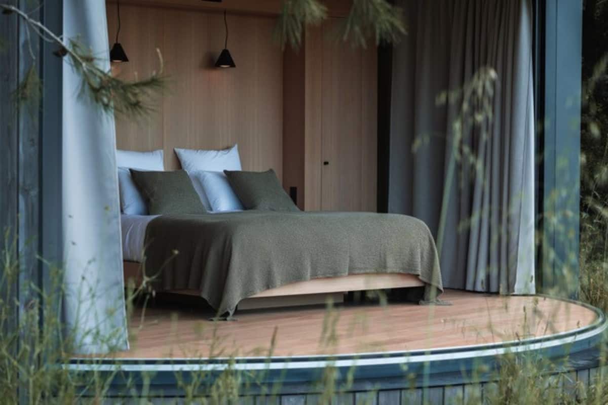 Uma cama redonda com base de madeira, roupa de cama com travesseiros e uma cortina.