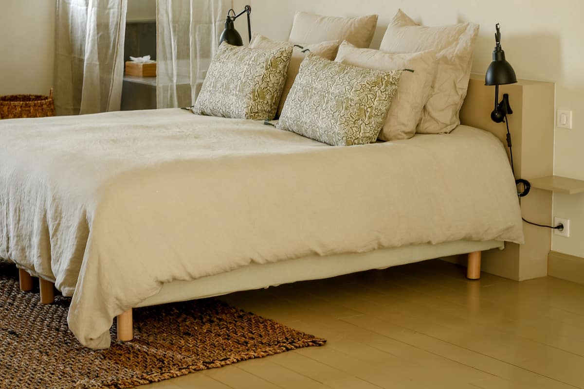 Quarto com cama grande, viga de madeira no teto, mesa de cabeceira e abajur.
