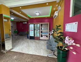 Lobby de hotel com balcão de recepção, área de estar e frigobar repleto de bebidas.