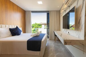 Quarto de hotel com uma cama, televisão, banheiro com bancada de mármore e vista para o verde lá fora.