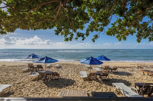 Uma praia com guarda-sóis e espreguiçadeiras, um deck de madeira e o oceano ao fundo.