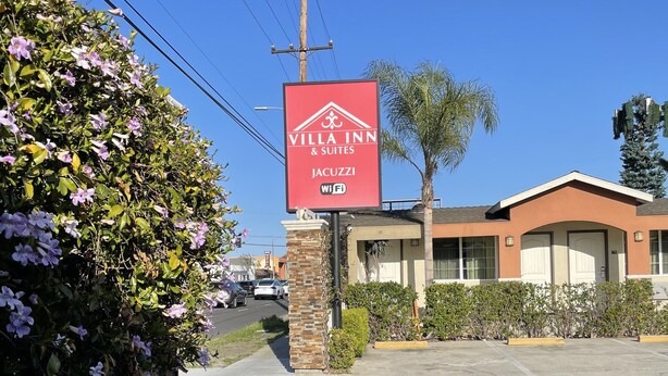 Placa da Villa Inn & Suites com um pilar de tijolos, cercada por vegetação e um céu claro.