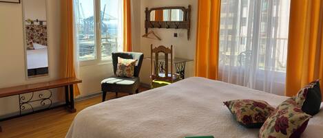 Quarto com cama, cadeira, mesa e janela com cortinas.