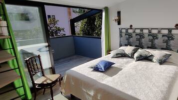 Um quarto com cama, cadeira, mesa de cabeceira e janela.