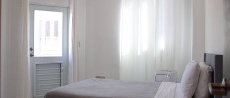 Quarto com cama, mesa de cabeceira, porta e janela com cortinas.