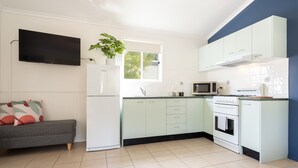 Uma cozinha moderna com armários brancos, micro-ondas embutido e fogão. Na área de estar adjacente, há um sofá cinza com almofadas coloridas.