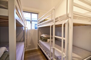 Quarto com beliche, janela, piso de madeira e porta branca.