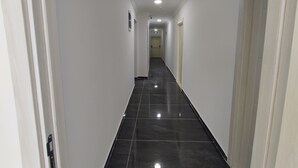 Um corredor comprido e estreito, com paredes brancas e piso preto brilhante.