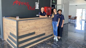 Um balcão de recepção com acabamento em madeira e uma parede preta com letras vermelhas. Há um extintor de incêndio vermelho na parede atrás do balcão.