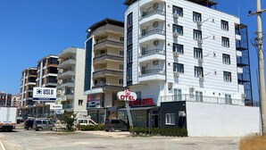 Um hotel com vários andares e varandas, um letreiro com o nome OTEZ HOTEL, e uma placa USLU indicando um comércio próximo.