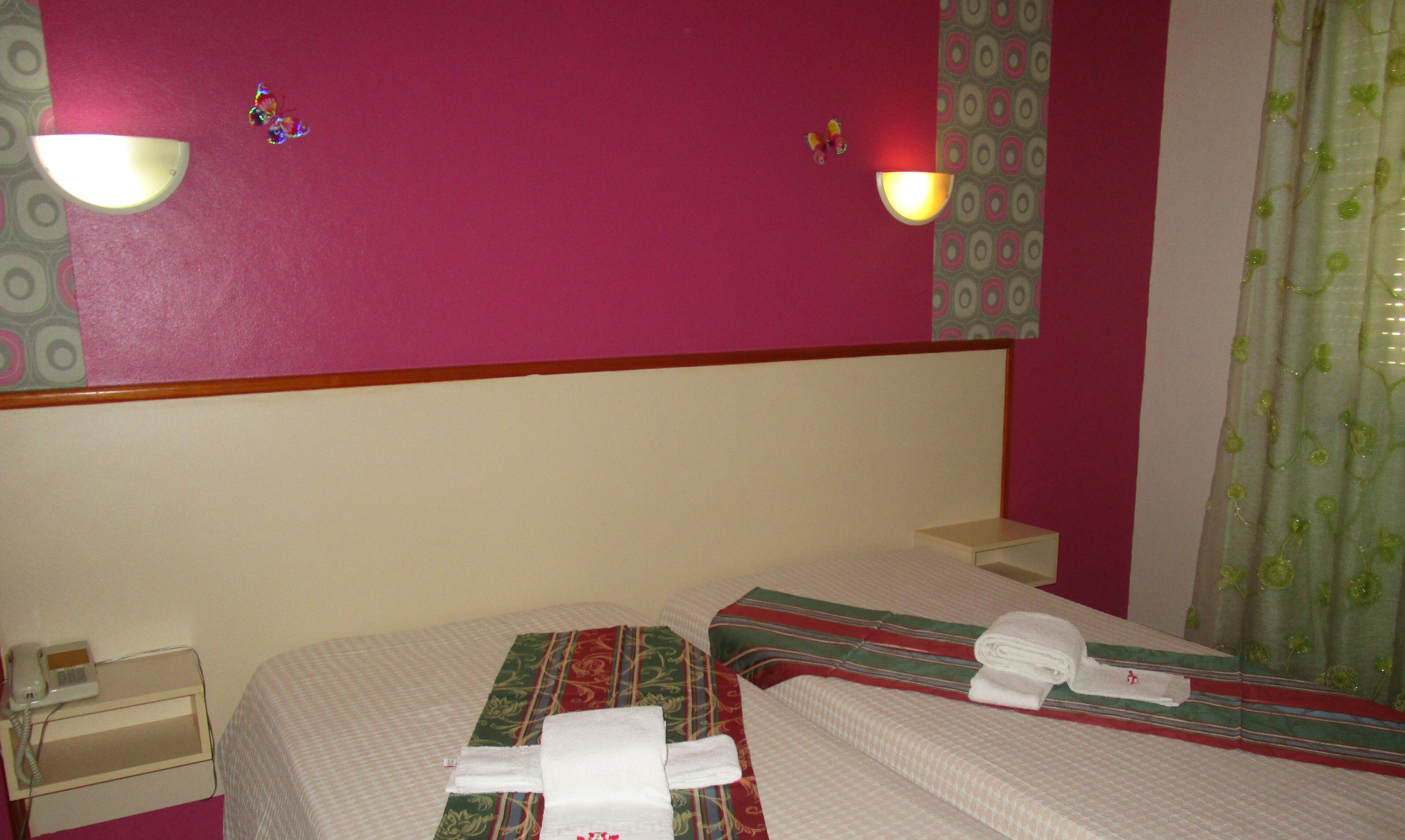 Quarto de hotel com duas camas, um telefone ao lado e cortina com padrão verde.
