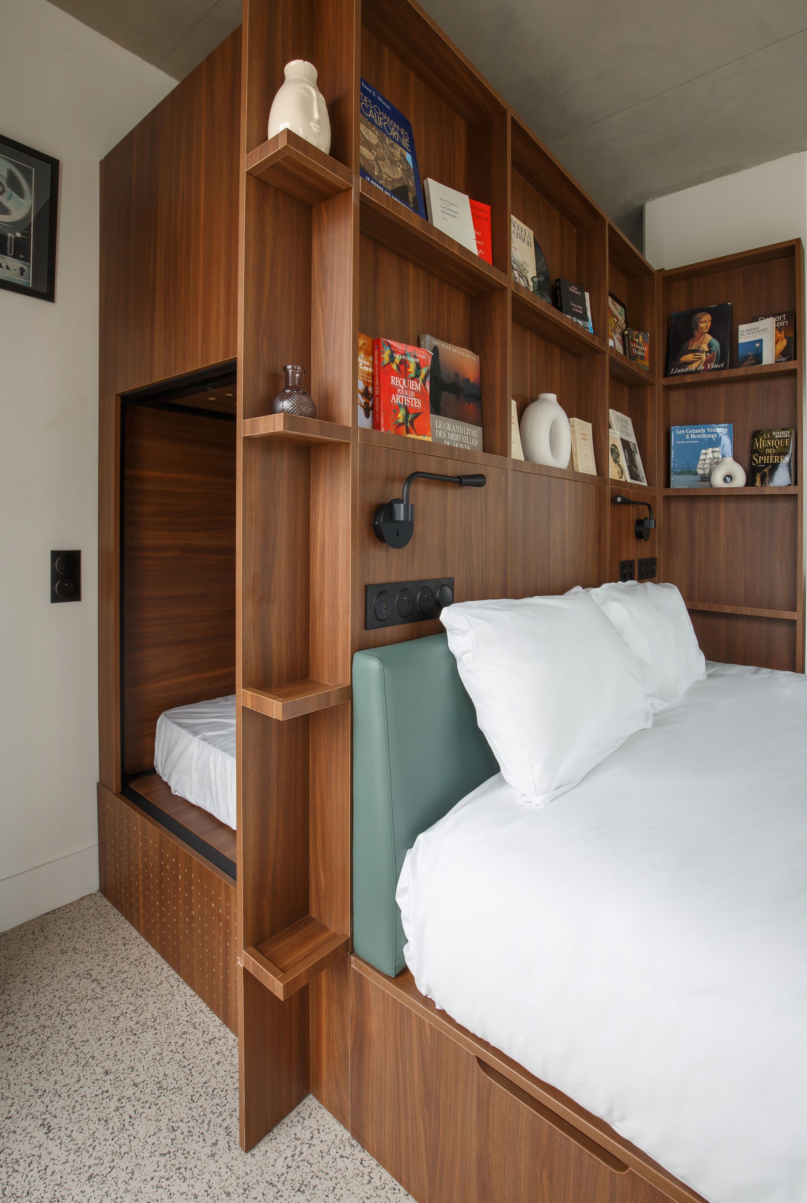 Quarto moderno com estante de madeira embutida, cabeceira estofada verde e cama branca.