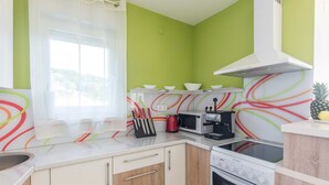 Cozinha equipada com micro-ondas, torradeira e fogão. Armários brancos e janela com vista para vegetação.