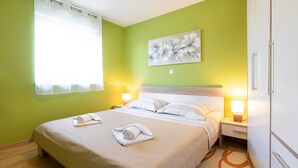 Cama bem arrumada com duas toalhas enroladas, um quadro na parede e abajures nas mesas de cabeceira.