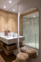 Uma casa de banho moderna com um espelho grande, duas lavatórios e uma cabine de duche com vidro.