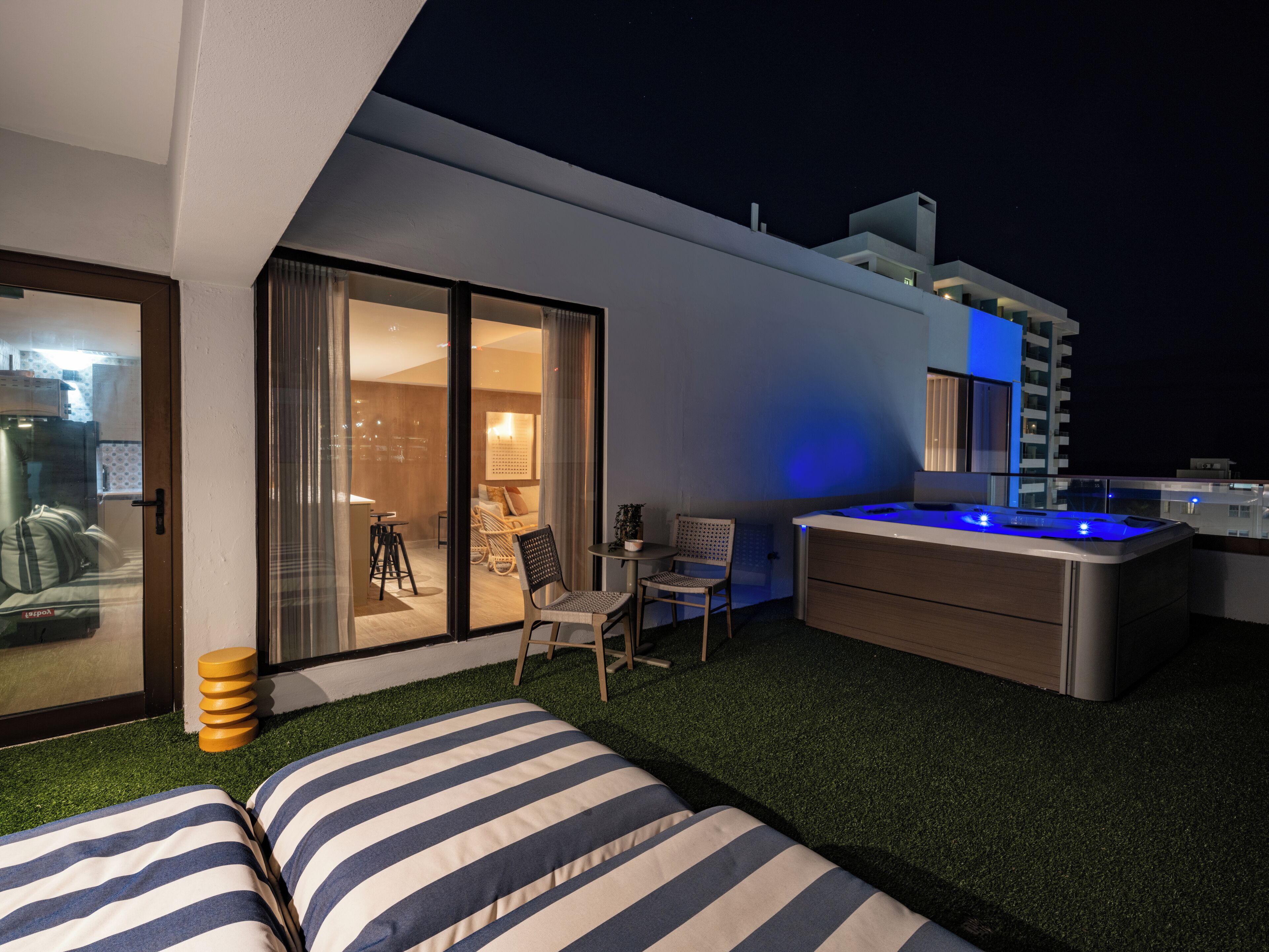 Uma área externa moderna com hidromassagem, assentos e vista da cidade à noite.