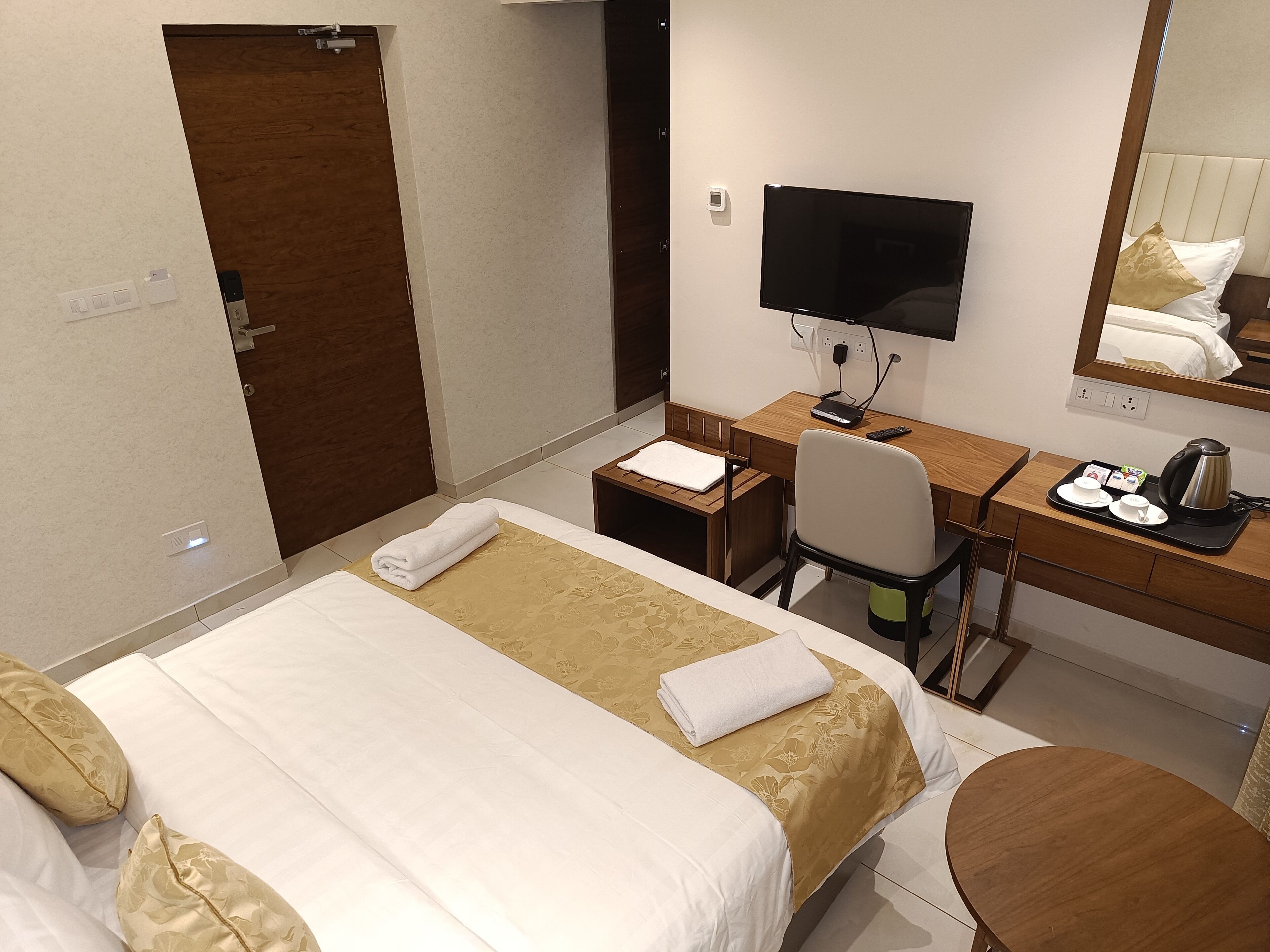 Quarto de hotel com duas camas, uma mesa com computador, uma cadeira, televisão e máquina de café.
