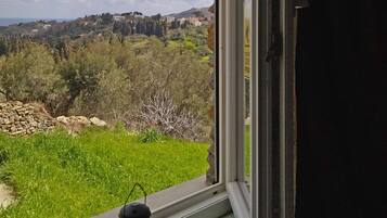 Janela com vista para uma paisagem verde, uma parede de pedra e um lampião preto no parapeito.