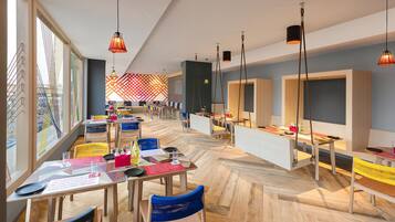Restaurante moderno com chão de madeira, cadeiras coloridas e luminárias pendentes. Mesas montadas com cardápios e copos.
