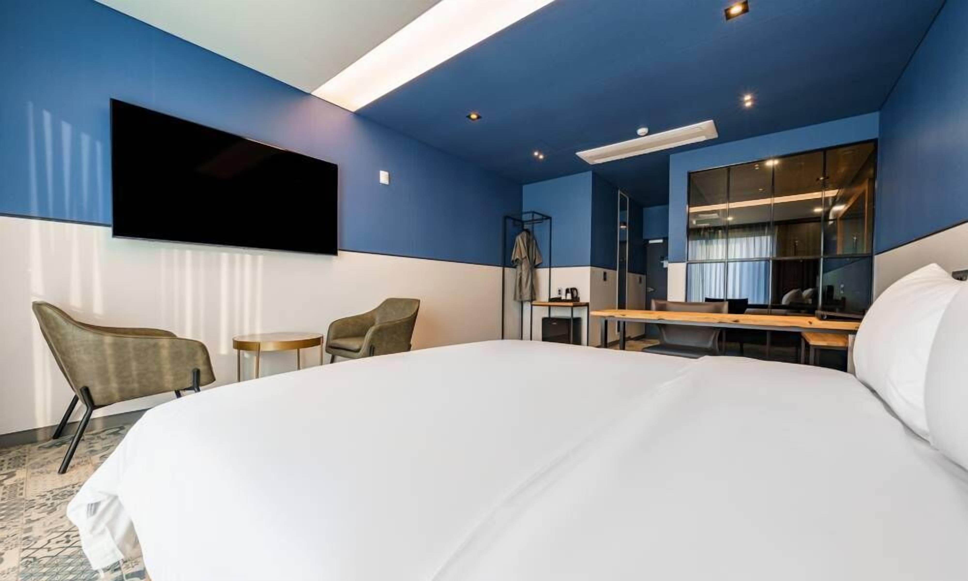 Quarto de hotel moderno com uma cama grande, uma escrivaninha, duas cadeiras, uma TV de tela plana e um espelho.