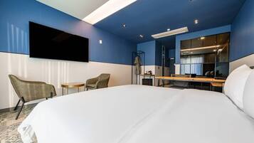 Quarto de hotel moderno com uma cama grande, uma escrivaninha, duas cadeiras, uma TV de tela plana e um espelho.