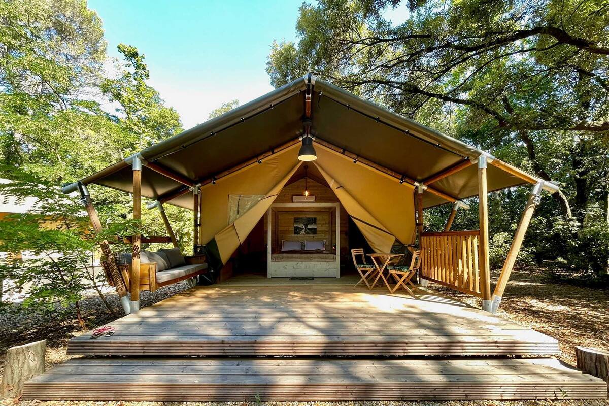 Uma cabana de madeira com varanda coberta, uma cama e uma mesa com cadeiras.