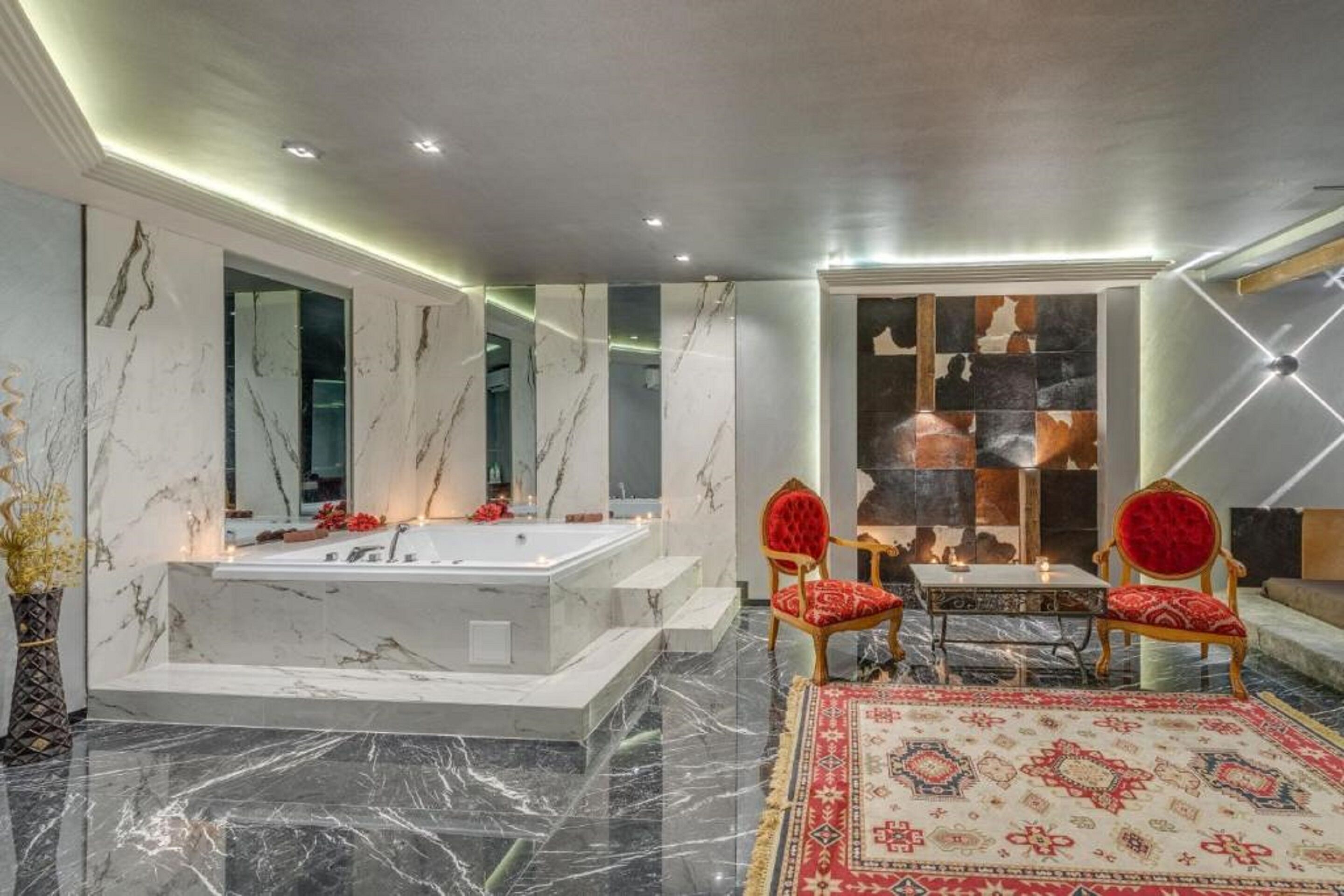 Um banheiro luxuoso com toucador de mármore, uma banheira grande e duas poltronas vermelhas estofadas.