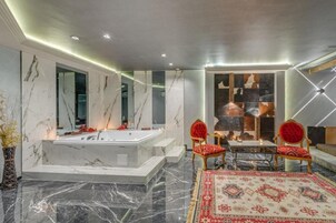 Um banheiro luxuoso com toucador de mármore, uma banheira grande e duas poltronas vermelhas estofadas.