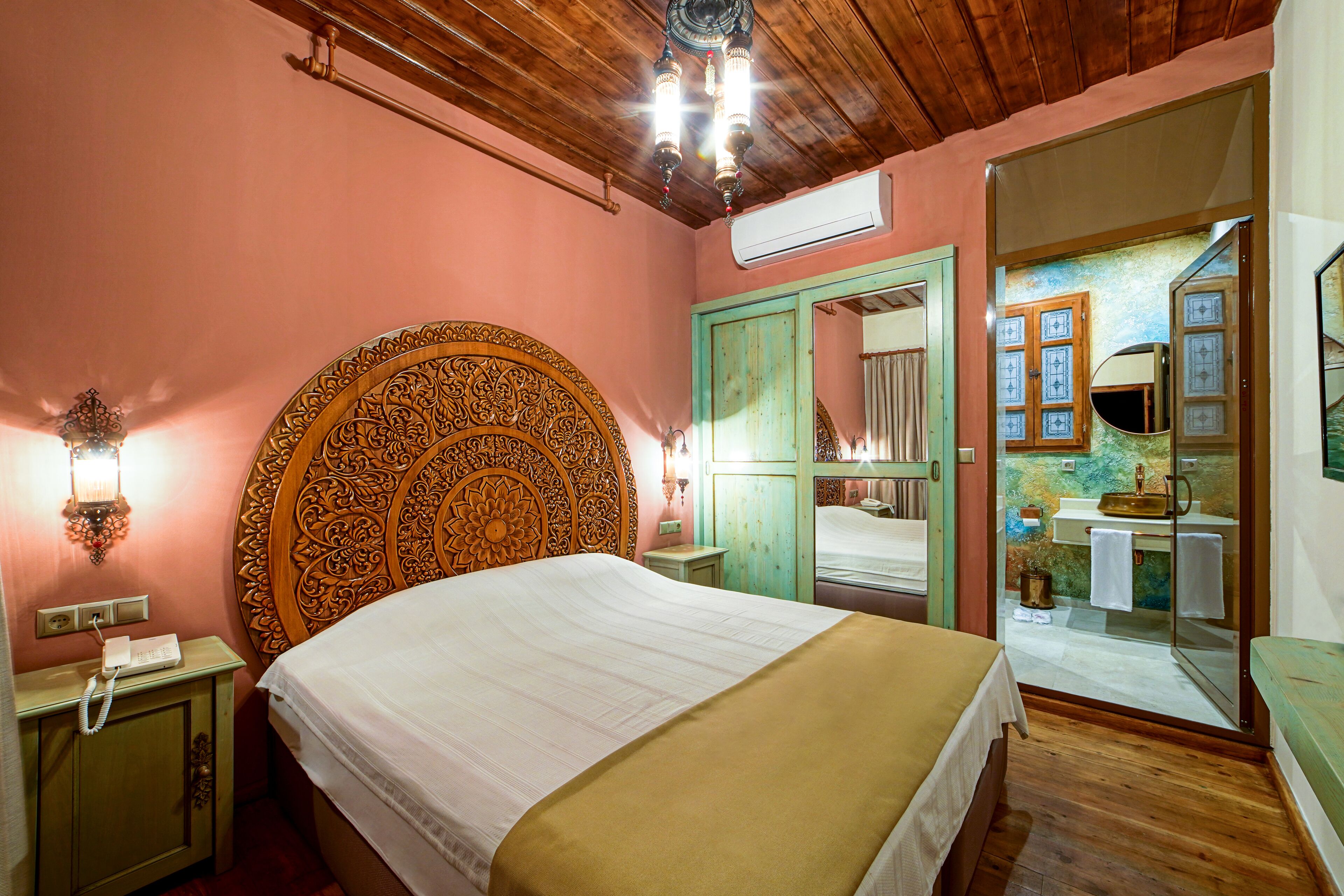 Quarto com uma grande cabeceira ornamentada, um telefone ao lado da cama e vista para o banheiro por uma porta aberta.