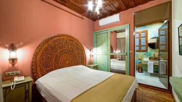 Quarto com uma grande cabeceira ornamentada, um telefone ao lado da cama e vista para o banheiro por uma porta aberta.