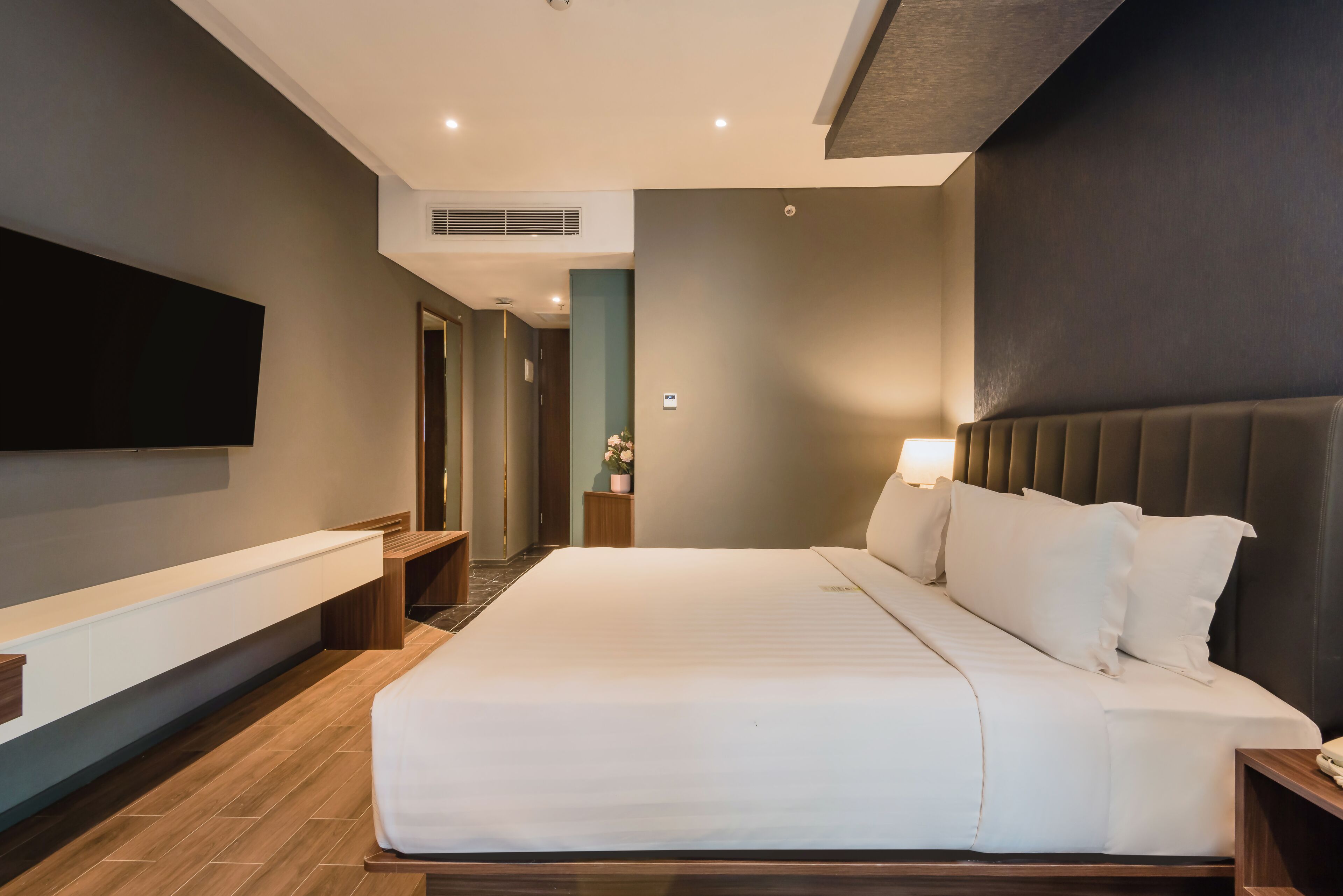 Quarto de hotel moderno com uma cama grande, televisão de tela plana na parede, mesa de cabeceira e criado-mudo.