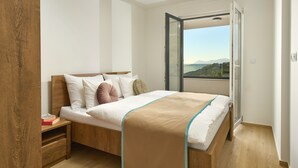 Quarto com cama de madeira, mesa de cabeceira, janela com vista para montanhas e porta deslizante.