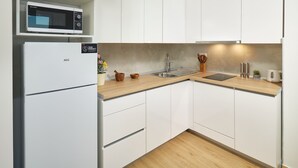 Uma cozinha moderna com armários brancos, uma pia de aço inoxidável, um micro-ondas e uma geladeira.
